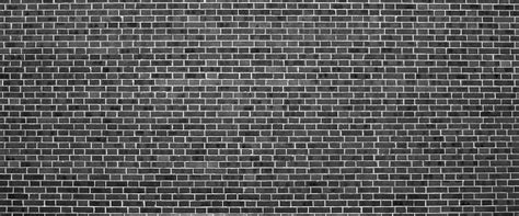 ฉากหลังสีเทาที่มีกําแพงอิฐสีดําเหมือนเก่า ชิ้นส่วนน้อยที่สุดของผนังอิฐระยะใกล้ พื้นหลั ภาพสต็อก