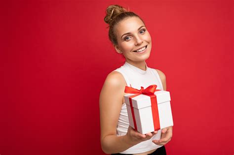 사진 촬영 아름다운 긍정적 인 미소 젊은 금발 의 여자 고립 된 빨간 배경 벽 위에 흰색 상단 을 들고 선물 상자를 들고 카메라를보고 경외감에 대한 스톡 사진 및 기타