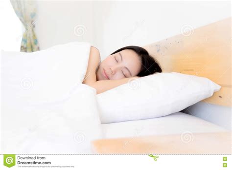 Женщина отдыхая в кровати с руками около ее головы на подушке Стоковое Фото изображение