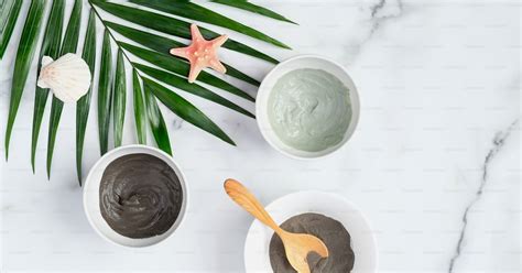 대리석 배경에 열대 야자 잎이 있는 그릇에 담긴 얼굴 점토 마스크와 파우더 얼굴 피부 관리 및 치료를위한 Spa 천연 유기농 화장품 플랫 레이 평면도 사진