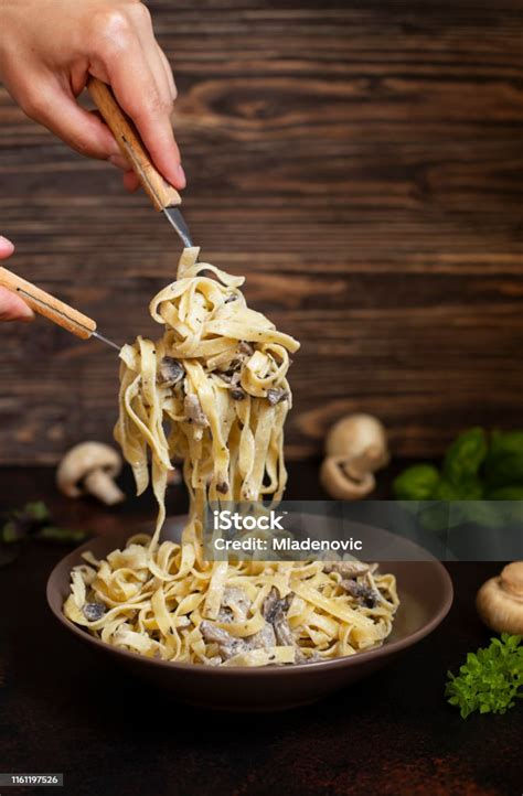 버섯과 크림 소스를 곁들인 홈메이드 이탈리안 페투치네 파스타 전통 이탈리아 요리 소박한 나무 배경이있는 어두운 테이블에서 제공됩니다 클로즈업 수직 스파게티 서버에 대한 스톡
