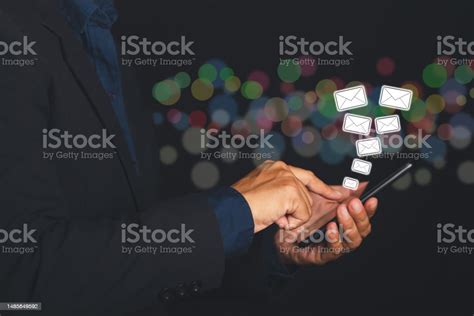 양복을 입은 사업가가 검은색 배경에 서 있는 동안 이메일 아이콘이 있는 스마트폰을 사용하고 있다 개념에 대한 스톡 사진 및 기타