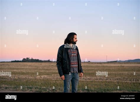 Caucasian Guy With Long Hair And Beard In Profile In The Middle Of A Large Grassy Field At