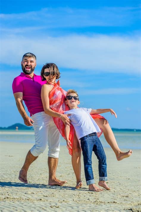 Семья из трех человек бежать вдоль тропического времени пляжа смеяться над и Enjoing совместно