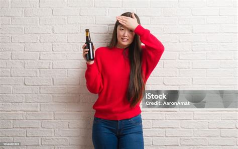 벽돌 벽 머리에 손으로 압박 하는 맥주를 마시는 동안 젊은 중국 여자는 수치심과 깜짝 얼굴로 충격 분노와 좌절 두려워 하 고 실수에 대 한 화가 마시기에 대한 스톡 사진 및