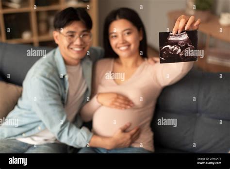 Cheerful Pregnant Korean Spouses Showing Ultrasound Photo Sitting At
