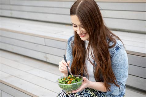 둥근 플라스틱 용기에서 샐러드를 먹고 나무 계단에 앉아 미소 그녀는 꽃 스커트 흰색 점퍼와 데님 재킷을 입고있다 25 29세에 대한 스톡 사진 및 기타 이미지 Istock
