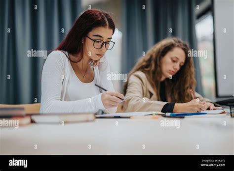 Two Female Students Focusing On Their Writing Assignments In Class