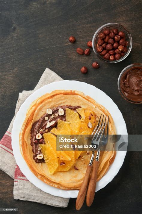 크레페 스게트 와 오렌지 초콜릿 스프레드 헤이즐넛 오렌지 슬라이스 과일을 화이트 플레이트에 넣고 오래된 어두운 나무 소박한 테이블 배경에서 아침 식사를 합니다 공간을