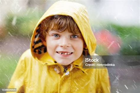 추운 날에 우산을 들고 진눈깨비 폭우 눈 속에서 학교로 가는 길에 아름다운 어린 아이 소년 컬러풀한 옐로우 코트 패션 캐주얼 한 옷을 입고 행복하고 즐거운 아이 비에 대한