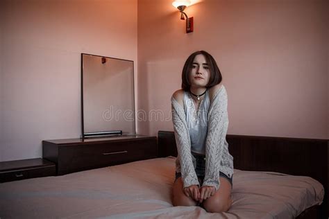 Молодая девушка в короткой юбке и белая блузка сидит на кровати с грустным и заботливым лицом