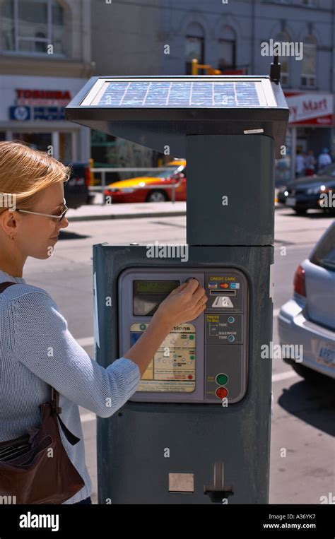 Woman Inputting A Coin Into A Solar Battery Powered Parking Meter