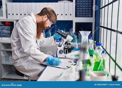 Young Redhead Man Scientist Using Microscope Writing Report Working At