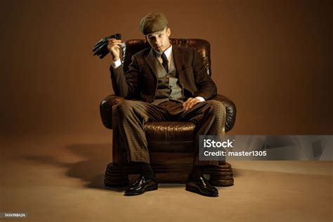 젊은 남자의 영화 초상화 복고풍 1920 년대 스타일의 영어 갱스터는 어두운 빈티지 배경에 고립 된 양복과 모자를 착용합니다