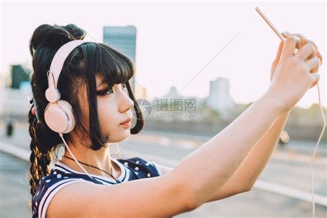 半长的年轻美丽的亚洲千禧女不循规蹈矩的户外城市背光用耳机听音乐高清图片下载 正版图片504961329 摄图网