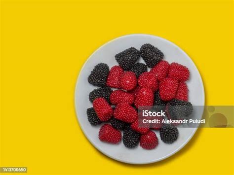 노란색 배경에 열매 형태의 빨간색과 검은 색 씹는 사탕 흰 접시에 나무 딸기 형태의 과자 마멀레이드 격리 아이들을위한 슬라이스