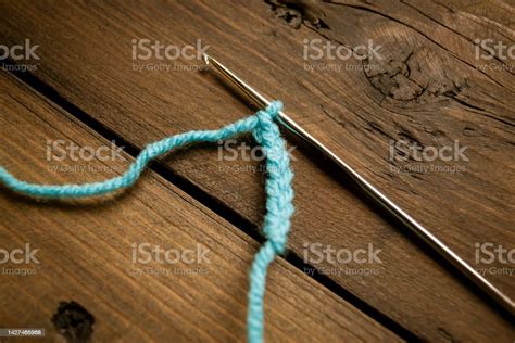 나무 테이블에 뜨개질로 후크 후크의 열에서 공기가 순환합니다 크로셰 뜨개질 루프의 첫 번째 행은 크로 셰 뜨개질됩니다 파란색 실로 크로 셰 뜨개질 0명에 대한 스톡 사진 및