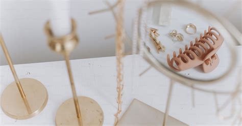 현대적인 황금 액세서리와 헤어 클립은 빈티지 양초가 있는 흰색 테이블에 보헤미안 거울에 반사됩니다 세련된 골드 링 체인 목걸이 귀걸이 머리핀 및 바렛 보호 주얼리