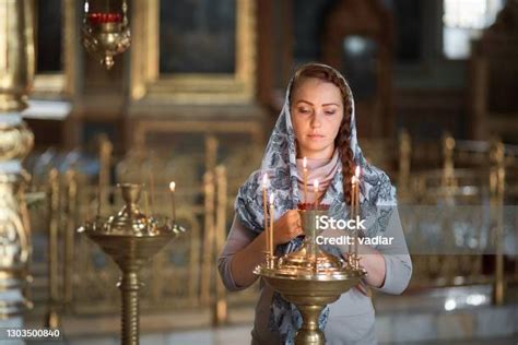붉은 머리와 머리에 스카프를 가진 러시아의 아름다운 백인 여성이 정교회에 있으며 촛불을 밝히고 아이콘 앞에서 기도합니다 교회에 대한 스톡 사진 및 기타 이미지 Istock