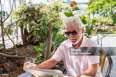흰 머리와 수염을 가진 아름다운 노인을위한 편안한 순간 뉴스를 읽고 테이블에 앉아 배경의 식물과 게이트 게이트에 대한 스톡 사진 및 기타 이미지 Istock