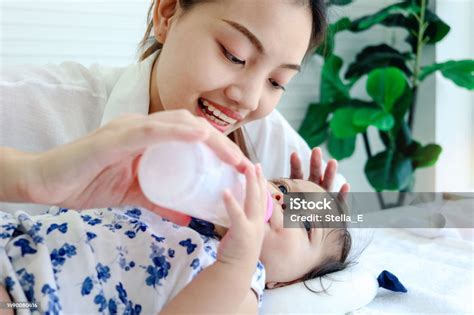 하얀 침대에 누워 있는 행복한 유아 아기 아기 엄마는 딸 아이에게 먹이를 주기 위해 우유병을 들고 있고 엄마는 새로운 가족을 사랑하고 돌보고 부모는 아이를 돌보고 어린