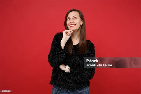 찾고 검은 모피 스웨터에 잠겨있는 젊은 여 자가 밝은 빨간색 벽 배경 스튜디오 초상화에 고립 된 턱에 손 버팀대를 올려 사람들이