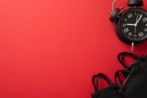 블랙 프라이데이 판매 개념 검은 색 알람 시계와 종이 봉지의 상단보기 사진 복사 공간이있는 고립 된 빨간색 배경에 벽 시계에