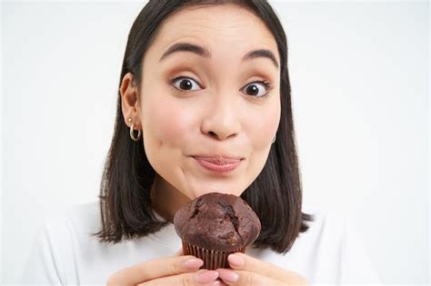 Free Photo Close Up Of Cute Smiling Asian Woman Holding Chocolate Cupcake Near Mouth Having