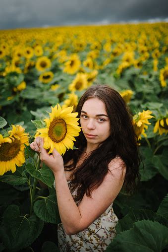 여자는 해바라기를 들고 자연을 즐기고 웃고 있다 해바라기 밭에 서 있는 젊은 아름 다운 여자입니다 일출이나 일몰에 쾌활한 소녀의 맑은 사진 여름철에 순간을 즐기십시오 근접