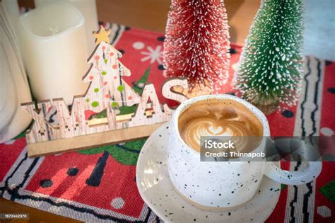크리스마스 장식과 나무 책상에 크리스마스 트리 싸구려가 있는 컵 머그잔에 라떼 아트 우유 거품이 있는 뜨거운 커피 라떼를 닫습니다 메리 크리스마스와 새해를 축하합니다 0명에