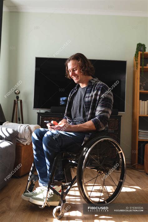 Caucasian Disabled Man Sitting On Wheelchair Smiling While Using Smartphone At Home Disability