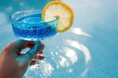 수영장 배경에 맛있는 파란색 칵테일 블루 라군과 노란색 레몬 한 잔 알콜 칵테일 육즙이 많은 과일 블루와 Curacao 리큐어 아이스 큐브 및 레몬 조각 0명에 대한 스톡