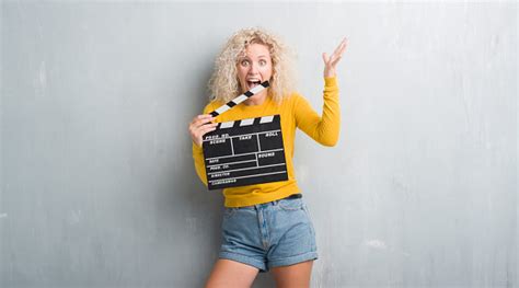 그런 지 위에 젊은 금발의 여 자가 회색 벽 Calpboard 영화 매우 행복 하 고 흥분 상자 식 축 하 승리 큰 웃음과 비명과 손을 잡고 감독에 대한 스톡 사진 및 기타