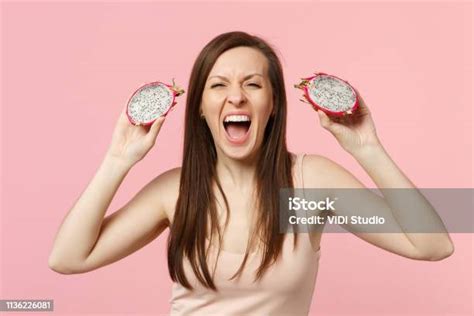 스튜디오에서 분홍색 파스텔 벽 배경에 고립 된 용 과일 신선한 잘 익은 피타 하 야의 두 개의 Halfs를 들고 미친 비명 젊은