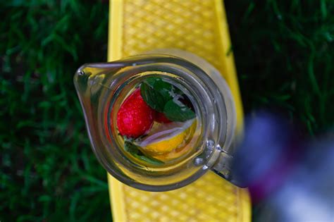 딸기 슬라이스 레몬 민트 잎을 곁들인 레모네이드 유리 주전자에 플라스틱 병에서 쏟아져 나오는 데포커스 스케이트보드 녹색 자연 배경 포커스가 부족합니다 감귤류 과일에 대한