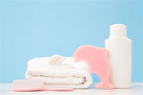 베이비 세탁 액세서리 분홍색 돌고래 스폰지 샴푸 병 헤어 브러시 흰색 수건 및 밝은 파란색 벽에 선반에 젖꼭지 파스텔 색상입니다 근접 촬영 전면 뷰입니다 텍스트의 빈