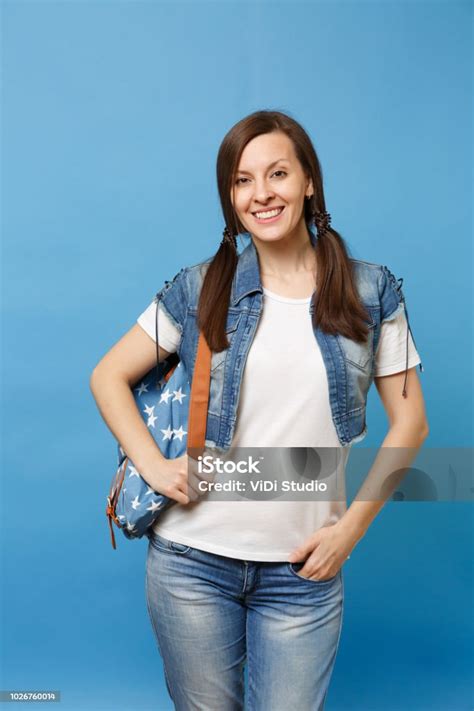 흰색 T셔츠 데님 옷 파란 배경에 고립 된 포켓에 손을 유지 하는 배낭에 젊은 웃는 예쁜 여자 학생의 초상화 고등학교에서 교육입니다 광고에 대 한 공간을 복사 합니다 20