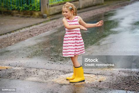 노란 장화를 신고 웅덩이를 걷는 행복한 미취학 소녀 화려한 옷을 입은 귀여운 아이가 웅덩이에 뛰어들고 물을 튀기고 야외 활동을