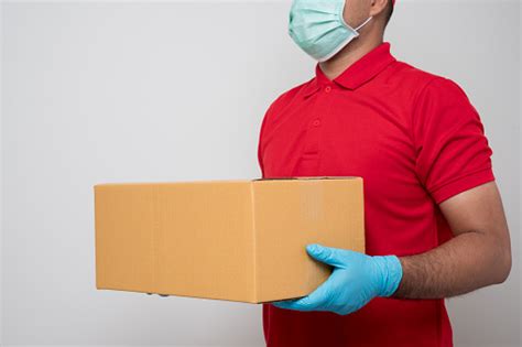 마스크와 고무 장갑을 착용한 빨간 배달 남자를 닫고 고객에게 보내는 소포 상자 골판지를 보관하는 것은 주의와 안전 전달 개념입니다 30 34세에 대한 스톡 사진 및 기타