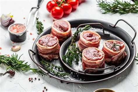 베이컨에 싸인 생 돼지 고기 메달리온 스테이크는 향신료 소금과 후추를 곁들인 가벼운 배경에 오래된 고기 트레이에 제공됩니다 긴