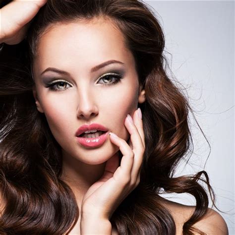 پرتره زن زیبای رسا با موهای مجعد قهوه ای بلند که روی پس زمینه تیره ژست گرفته است 1581109