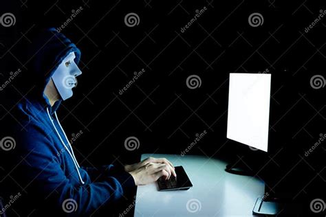 masked hacker under hood using computer to hack into system and trying to commit computer crime