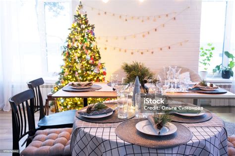 크리스마스와 새해를 위해 장식된 로프트 하우스의 현대적인 인테리어에서 접시 포크 나이프 냅킨 안경이 클로즈업된 축제 테이블을 제공합니다 축제 저녁 식사를 위해 손님을