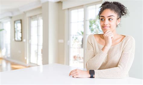 집에서 테이블에 앉아 아프리카 머리와 아름 다운 젊은 아프리카계 미국인 여자는 교차 팔과 손 턱에 제기와 미소와 함께 카메라에