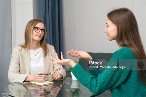 여자는 동료와 상담하여 중요한 논문을 종이에 태블릿에 씁니다 기자는 집에서 의자에 앉아 인터뷰를합니다 뒤에서 본 모습 두 아름다운 소녀의 의사 소통 서류 가방에 대한 스톡