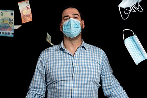 격자 무늬 셔츠와 수술 용 마스크를 입은 잘생긴 수염을 가진 남자는 유로 지폐와 수술 용 마스크가 주위를 날아다니는 코로나 바이러스로부터 자신을 보호합니다 35 39세에