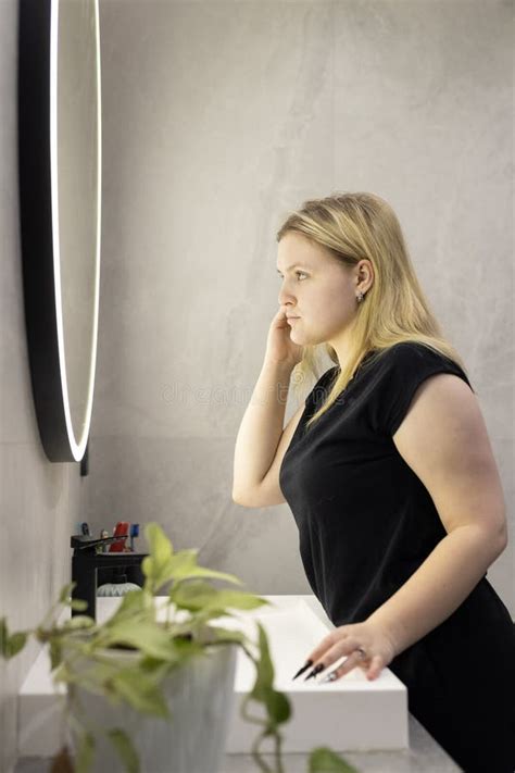 A Blonde Young Woman Touches Her Hair While Standing Near A Modern