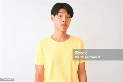 노란색 캐주얼 티셔츠를 입은 중국인 남성이 고립된 흰색 배경 위에 서 있는 모습이 얼굴에 진지한 표정을 짓고 있다 카메라를 보는 간단하고 자연스러운 스튜디오 촬영에 대한