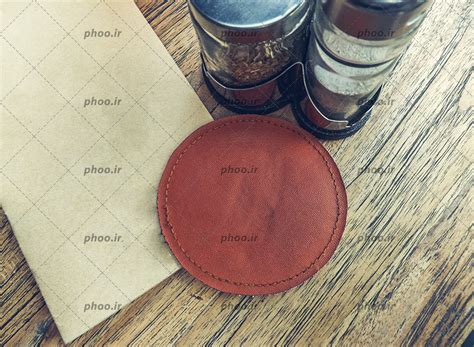 عکس با کیفیت کاغذ خالی در کنار زیر لیوانی چرمی قهوه ای در پس زمینه چوبی عکس با کیفیت و تصاویر