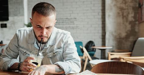 데님 재킷을 입은 젊은 수염 난 남자가 카페에 앉아 차가운 커피를 마시며 지도를 사용하여 방문하기 가장 좋은 장소를 찾고 있다